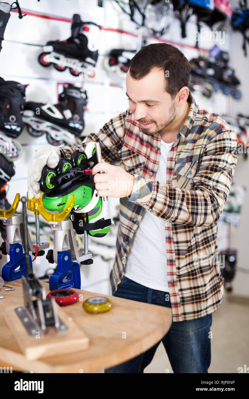 Smiling adult guy master fixing roller-skates in sports store Stock ...