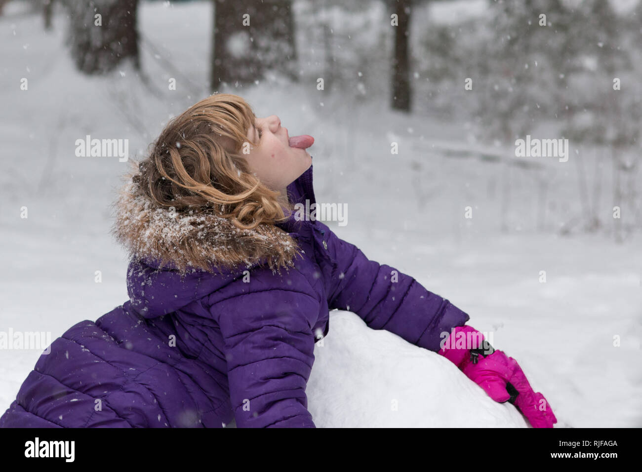 An eight-year-old girl playing in the snow sticks out her tongue to ...