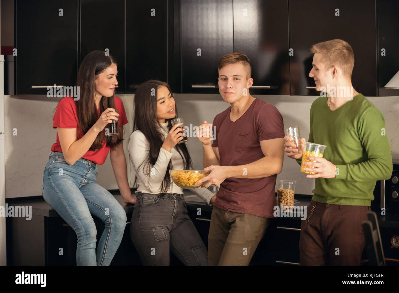 Four young friends standing on kitchen spending time together. Eating ...