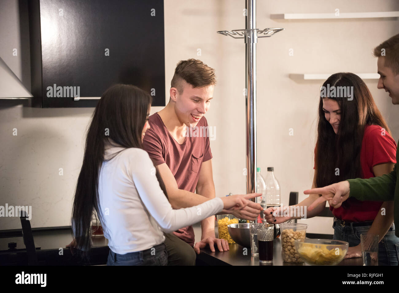 Four young friends standing on kitchen spending time together. Spiling ...
