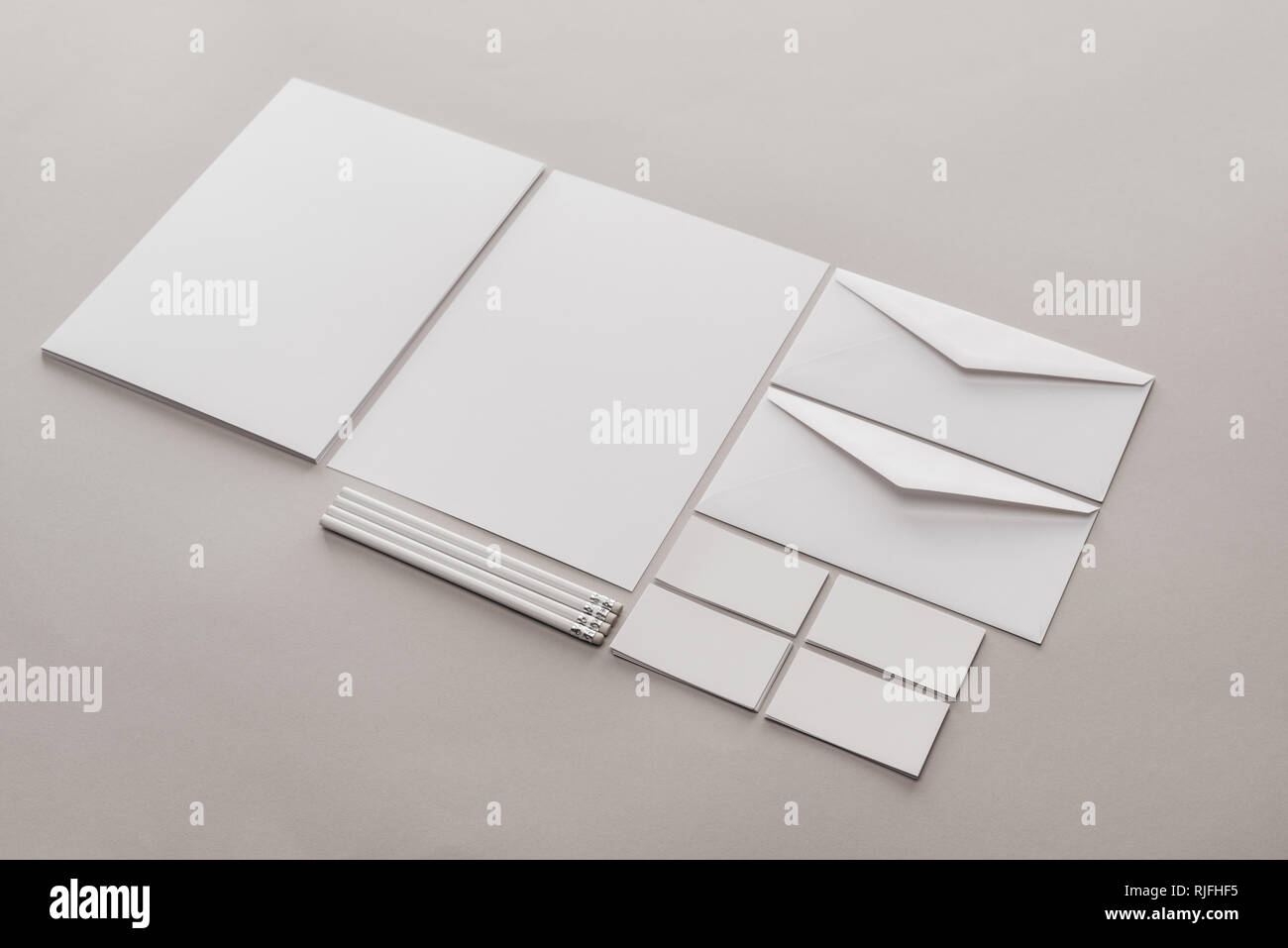 flat lay with white empty papers, cards, envelopes and pencils on grey ...