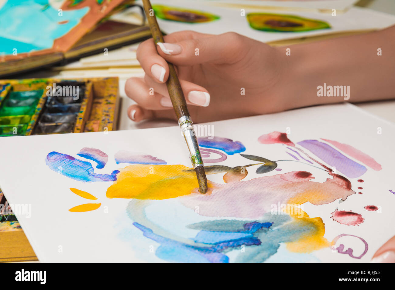 selective focus of female hand drawing on paper with watercolor paints ...