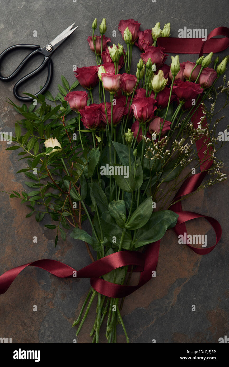 beautiful red eustoma flowers with ribbon and scissors on dark surface ...