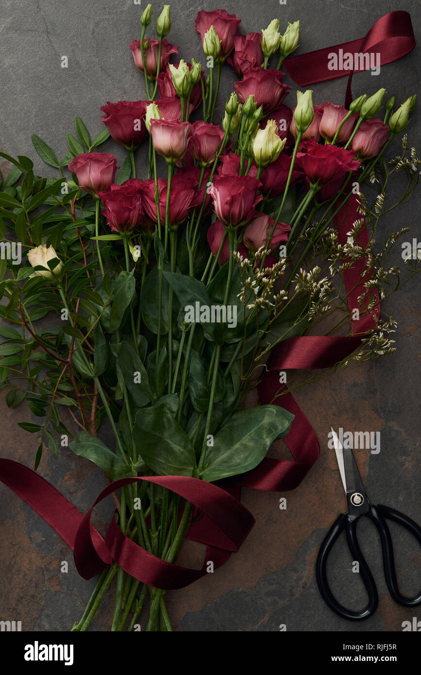 top view of beautiful red eustoma flowers with ribbon and scissors on ...