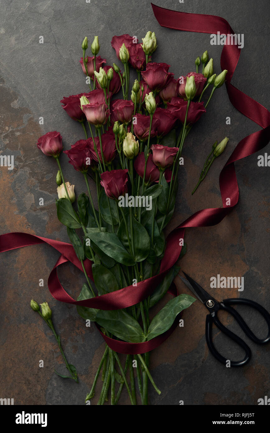 top view of beautiful red eustoma flowers and scissors on dark surface ...