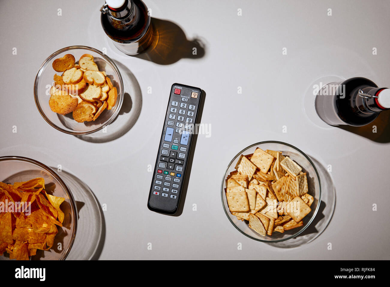 top view of bottles with beer near remote control and snacks on white ...