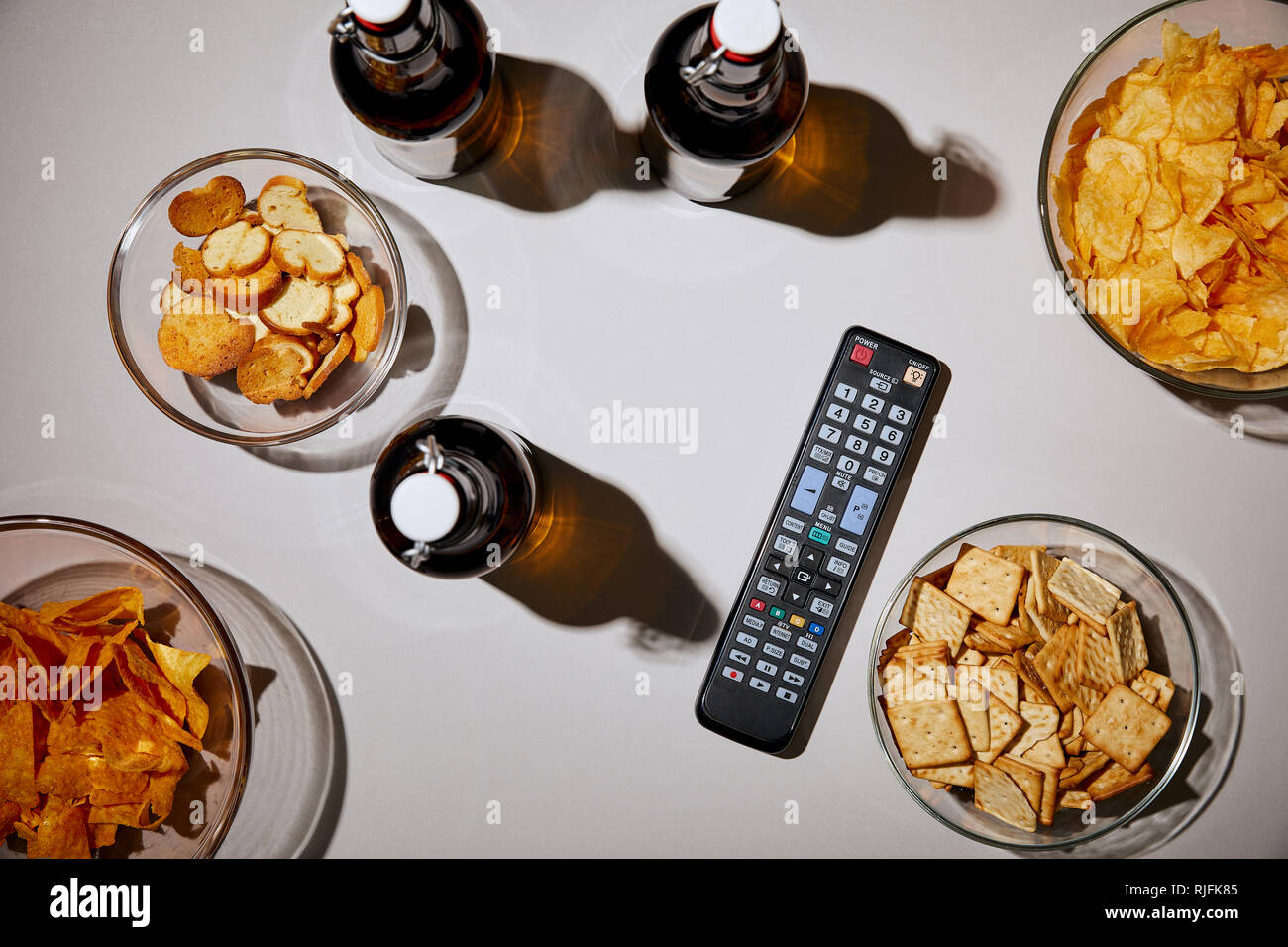 top view of bottles with beer near remote control and snacks in bowls ...