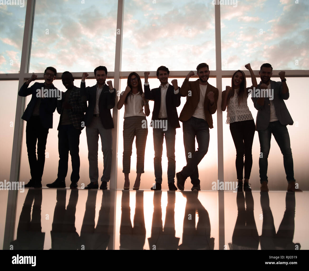 group of young professionals standing in an office with a large window ...