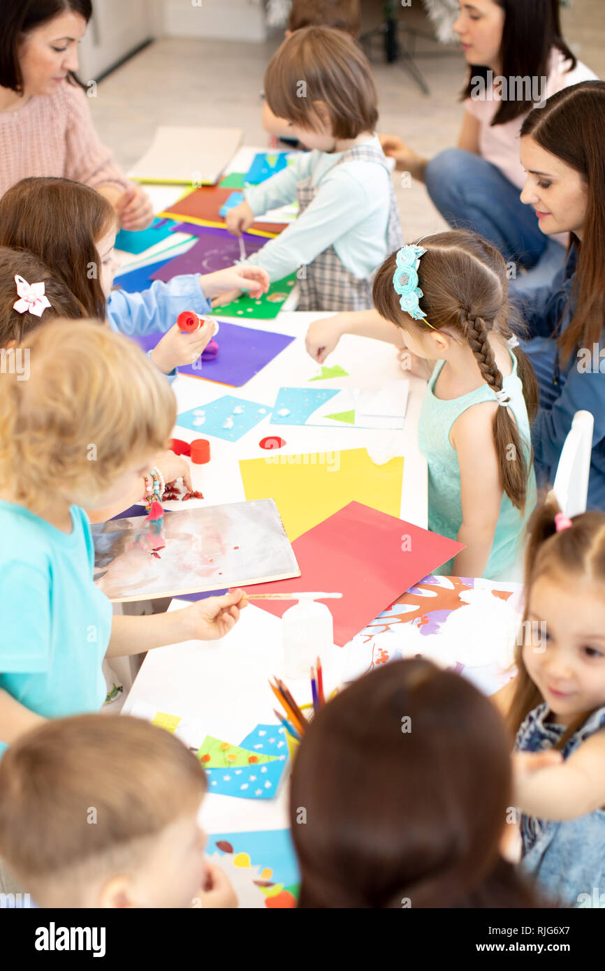 Group of preschool kids working with color paper, sciccors and glue on ...