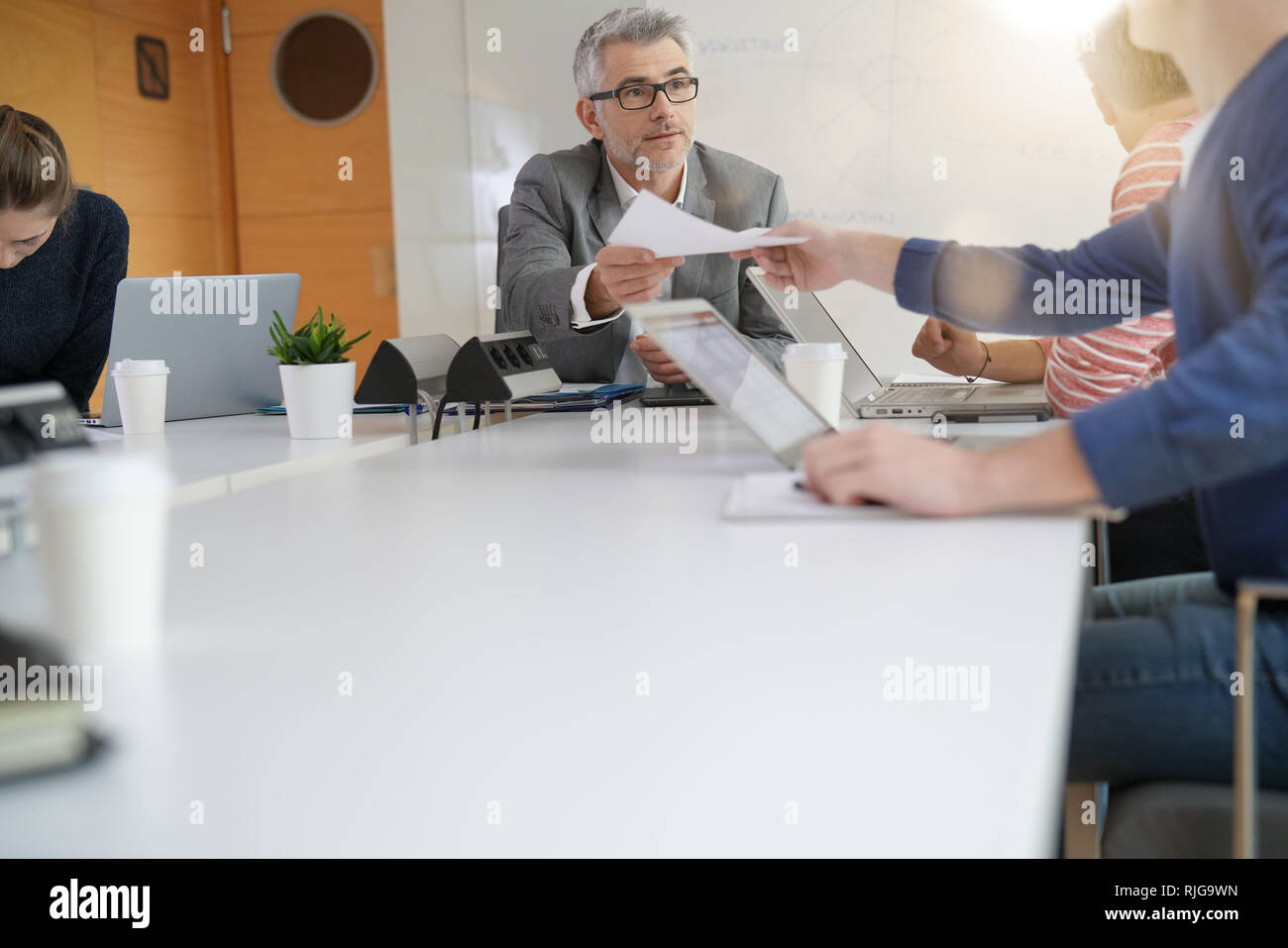 Teacher giving copies to students around table Stock Photo - Alamy