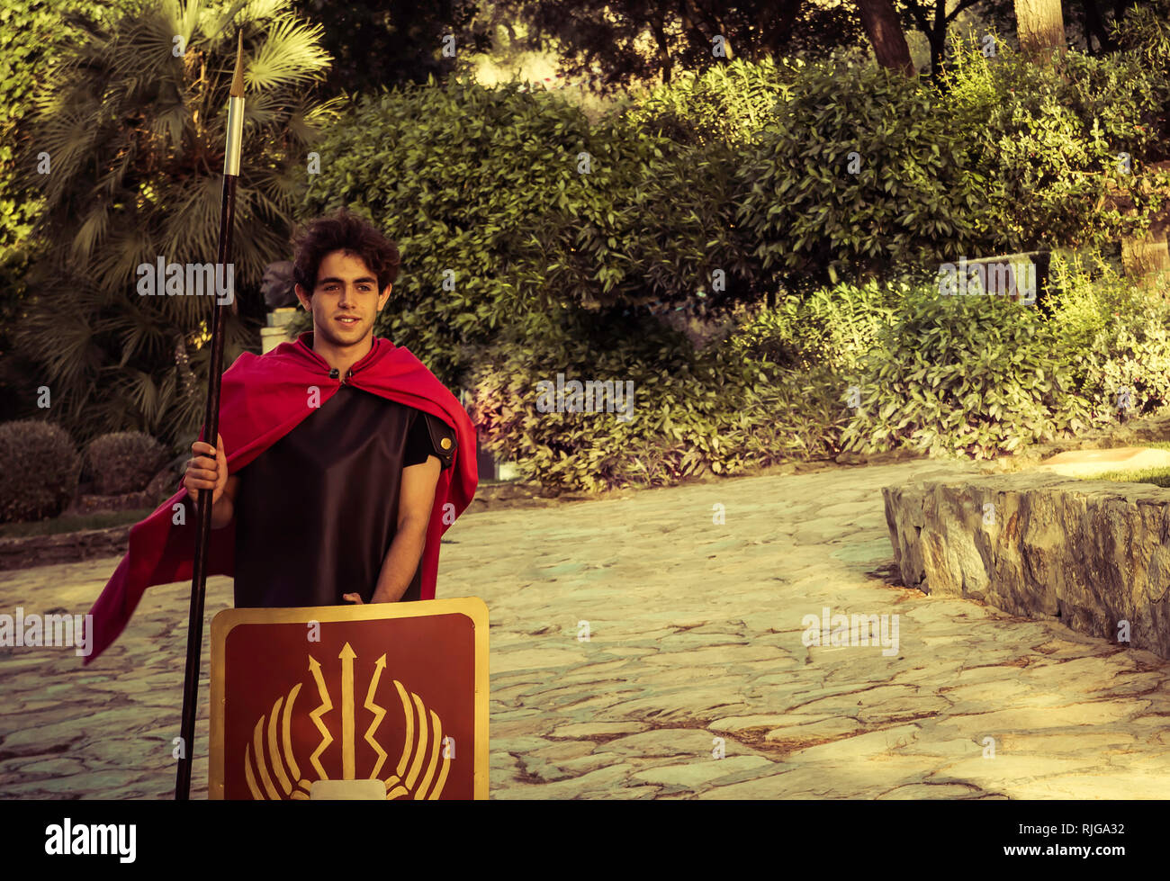 A pretty young man standing dressed like an ancient roman with a spear ...