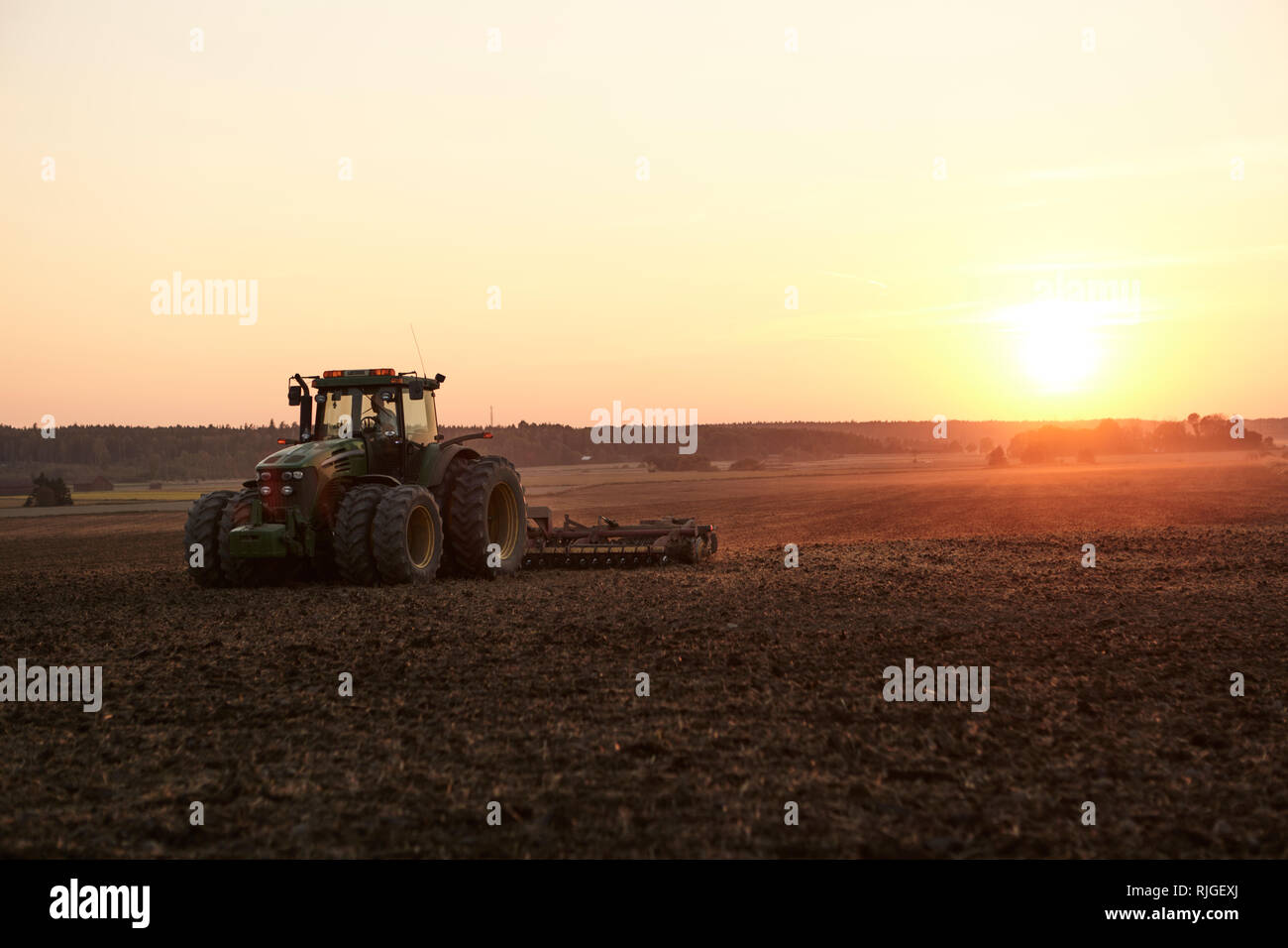 Tractor on field at sunset Stock Photo - Alamy