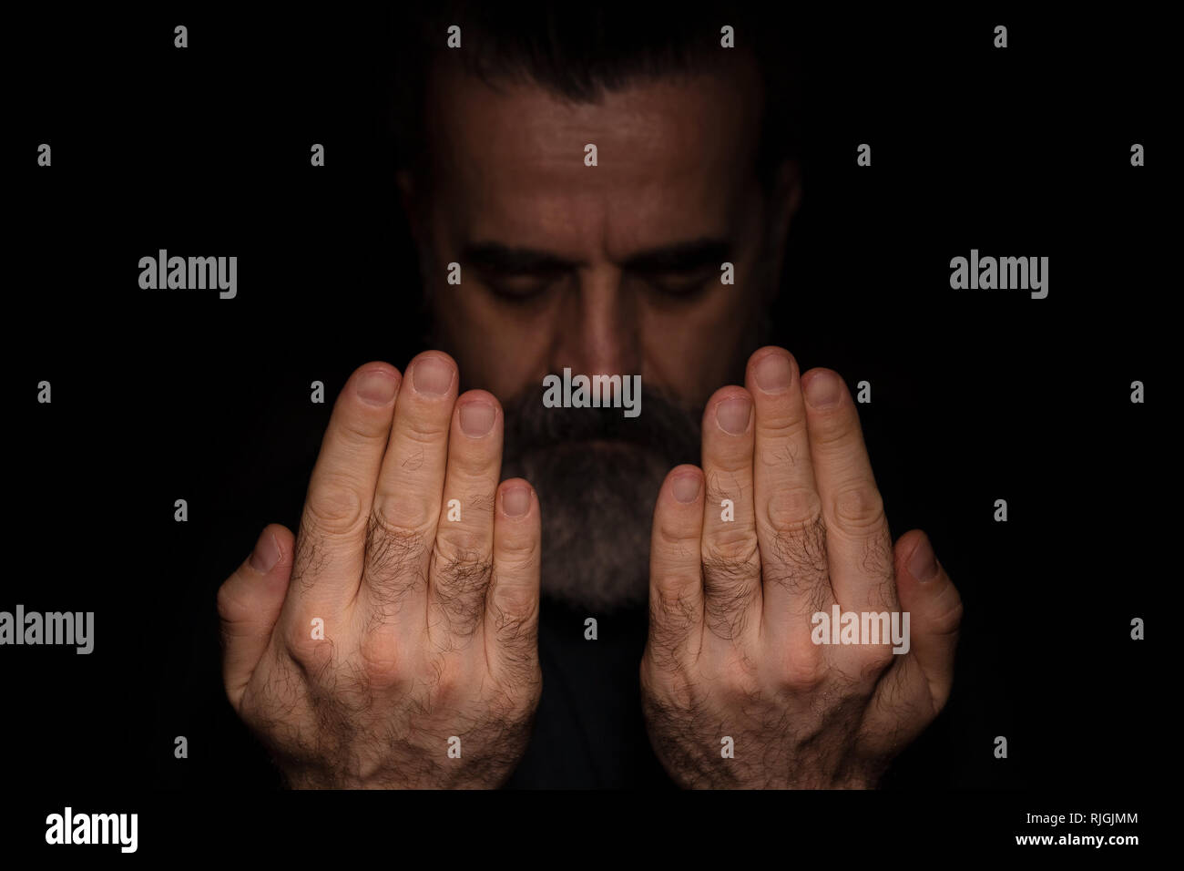 Man raising hands in prayer, in a dark room and with black background ...