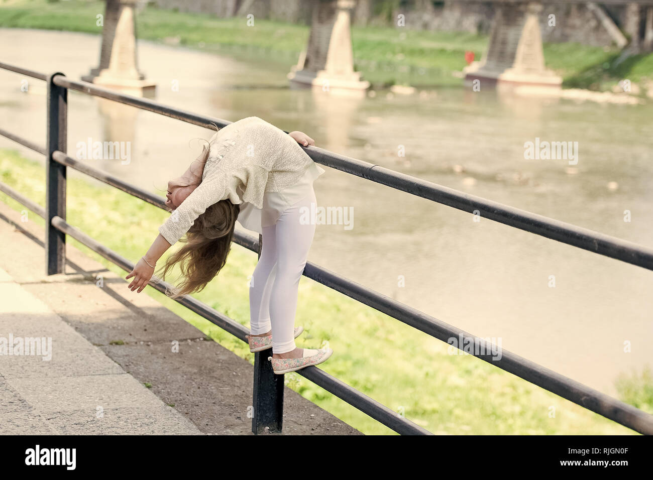 Kid girl bends backwards as flexible gymnast near railing at riverside ...