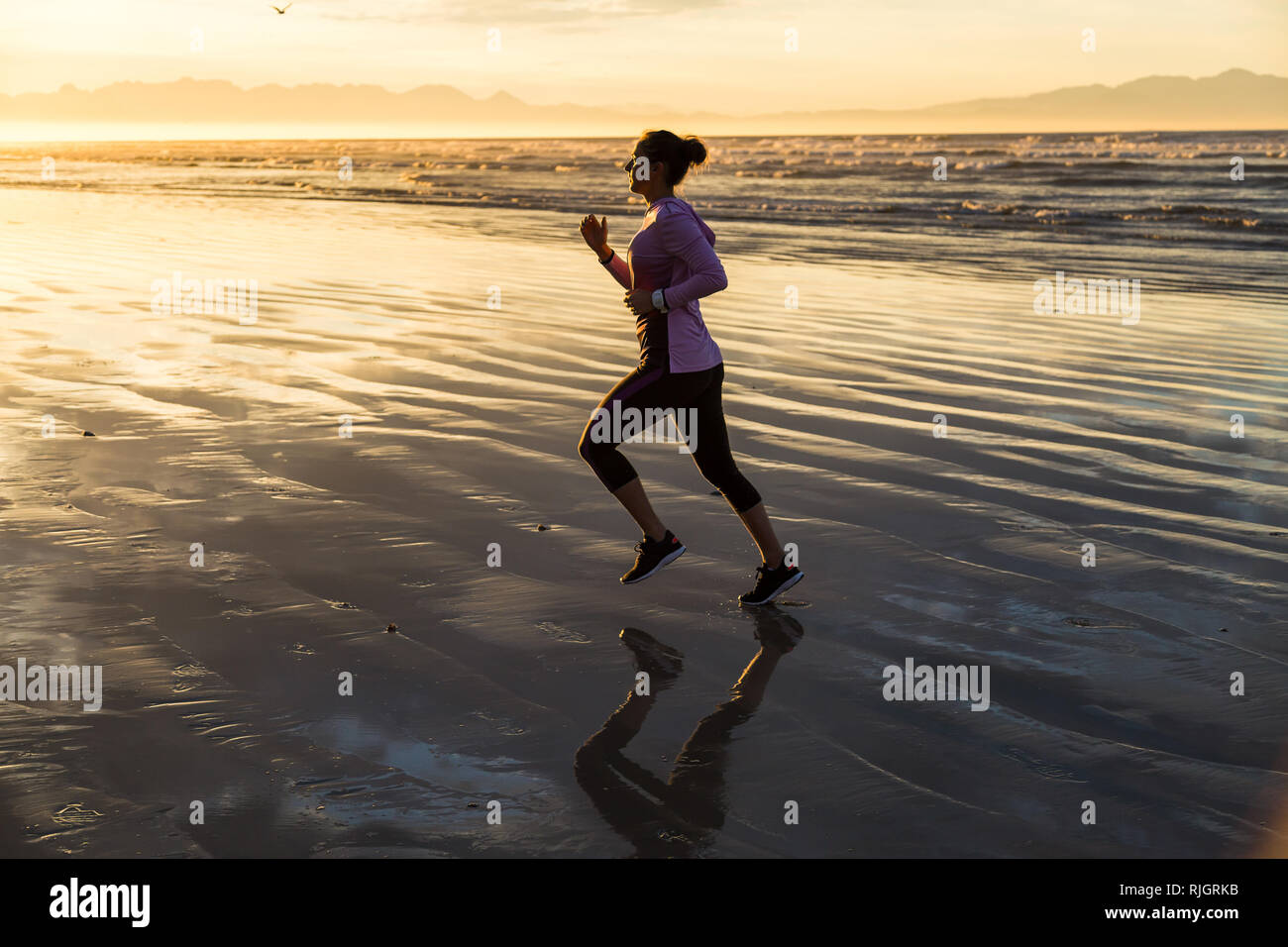 Young female runner jogging on a beach at sunrise Stock Photo - Alamy
