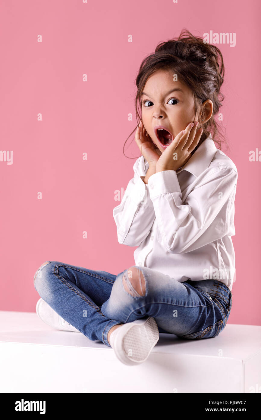 Cute scared surprised little girl in white shirt with hairstyle looking ...