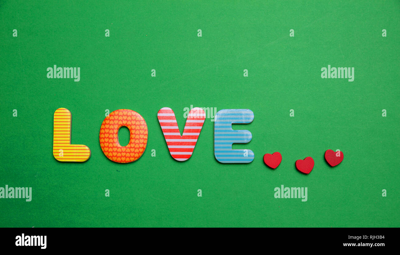 Love text with colorful letters and small red hearts on green color ...