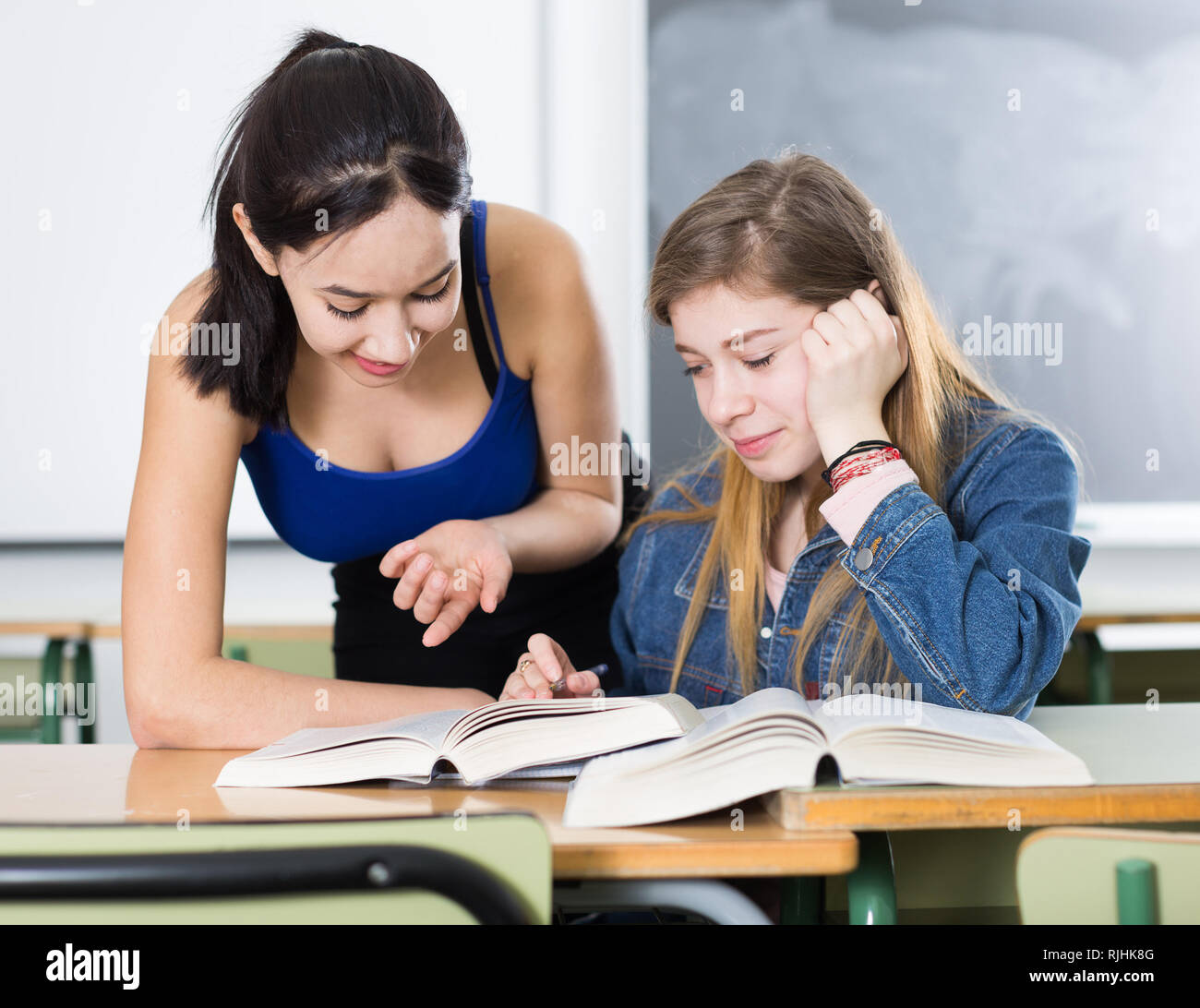 Girl is helping girlfriend with homework at the desk in the classroom ...