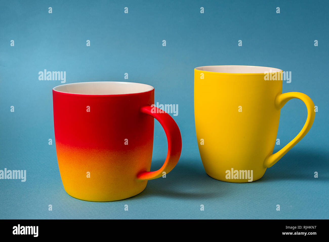 Big yellow and red mugs isolated on blue background, horizontal ...