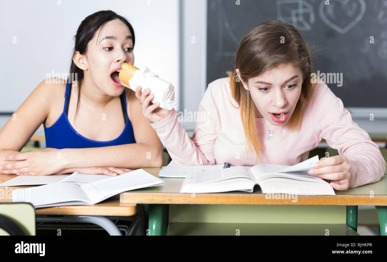 Smiling schoolgirls are learning at the desk and eating in the class ...