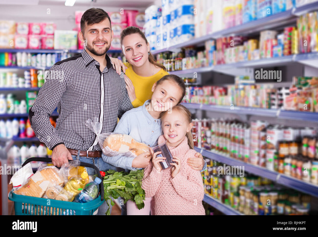 portrait of glad parents with two little girls with purchases during ...