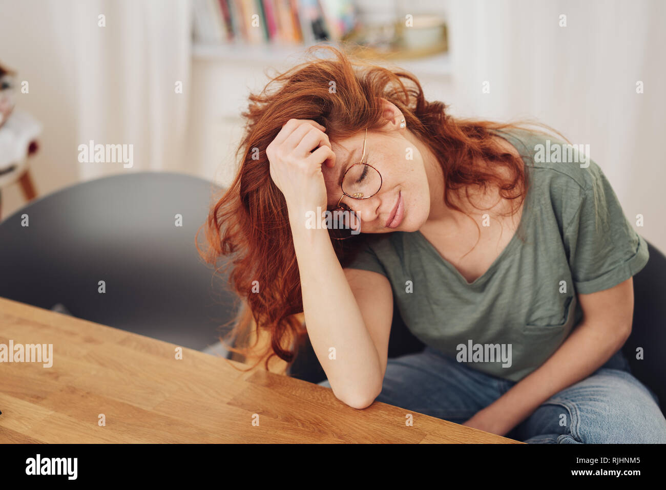 Young woman relaxing sitting at a table with eyes closed, her head ...