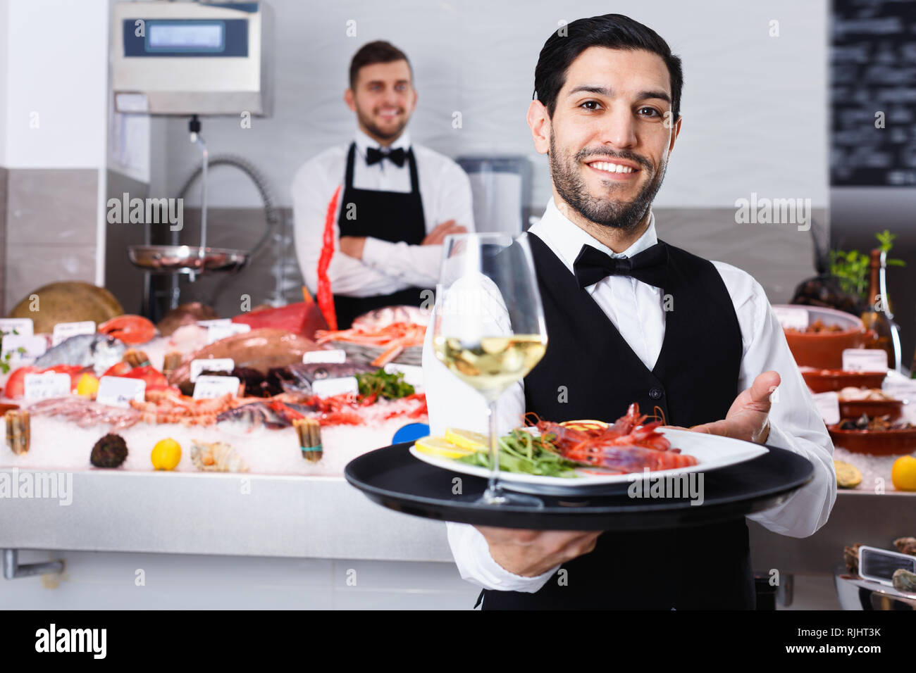 Glad waiter holding tray with seafood dishes at fish restaurant against ...