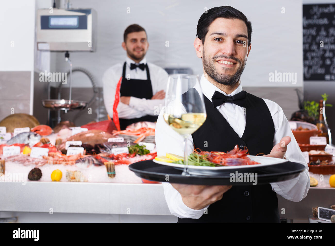 Portrait of smiling waiter with serving tray offering dishes in fish ...