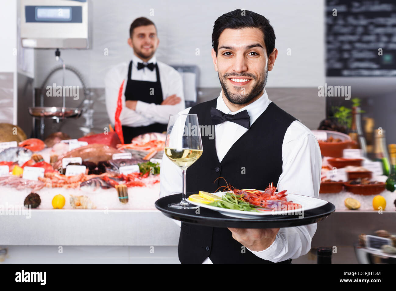 Glad positive waiter holding tray with seafood dishes at fish ...