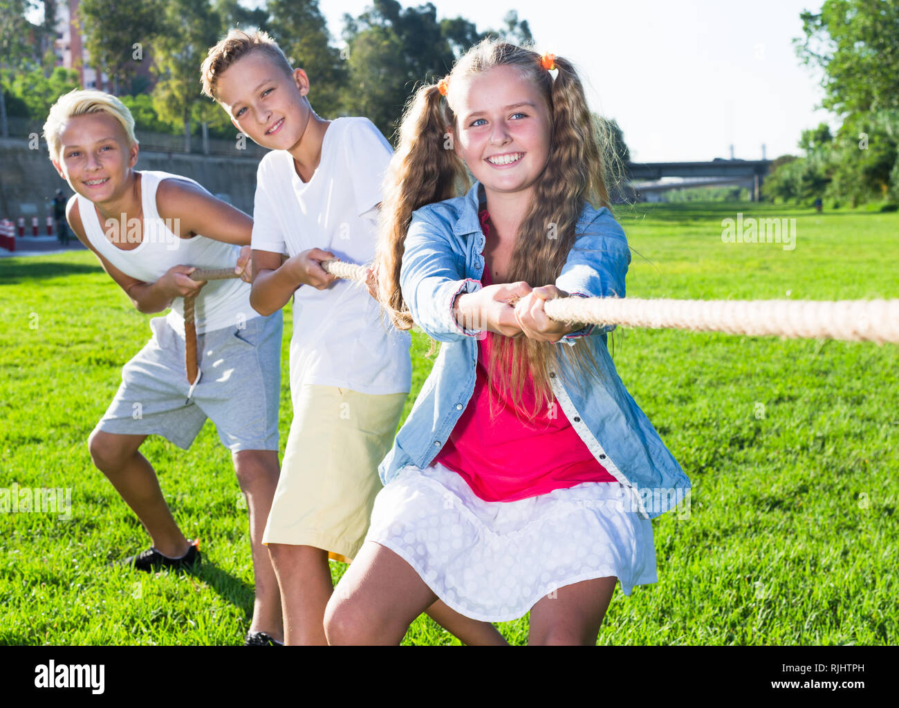 Group of laughing children having fun together outdoors pulling rope ...