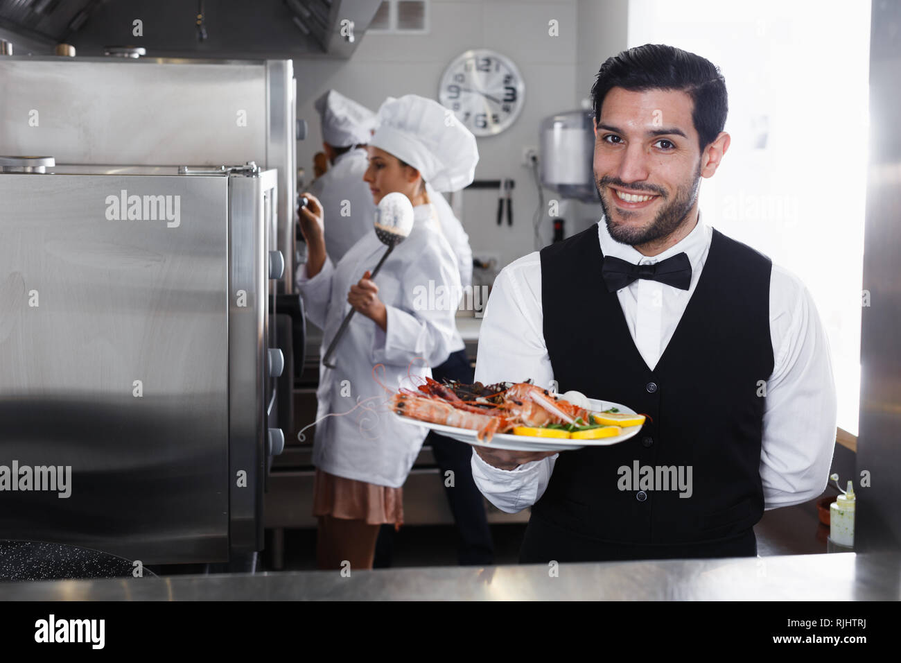 Portrait of handsome waiter with dish of seafood in kitchen on fish ...