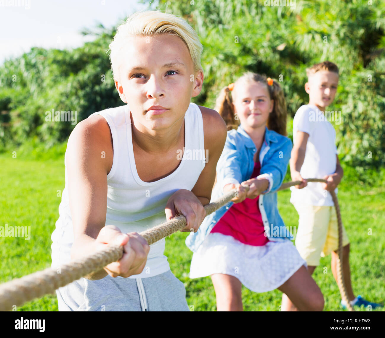 Group of laughing children having fun together outdoors pulling rope ...