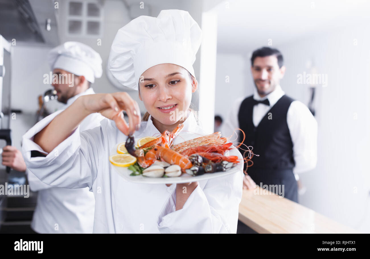 Female chef checking seafood dish in kitchen of restaurant before ...