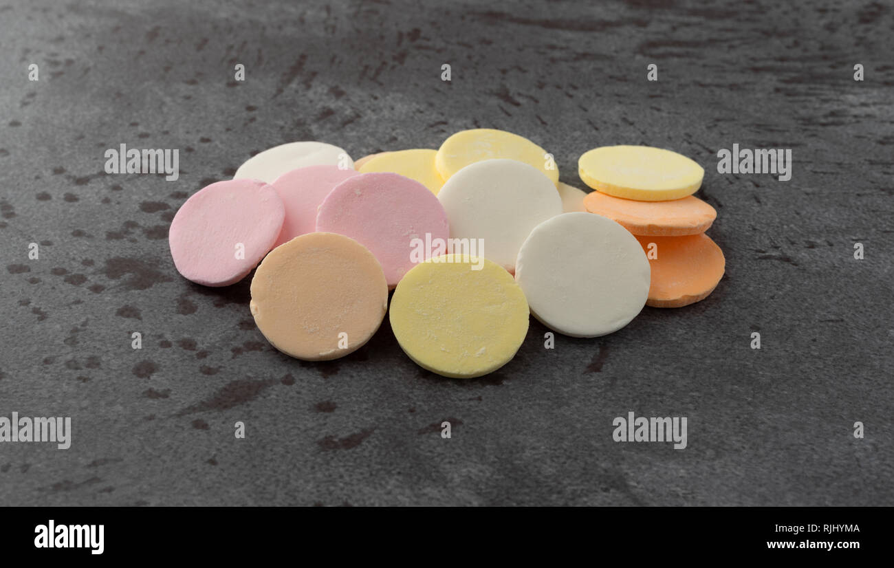 Several thin colorful candy wafers on a gray background illuminated ...