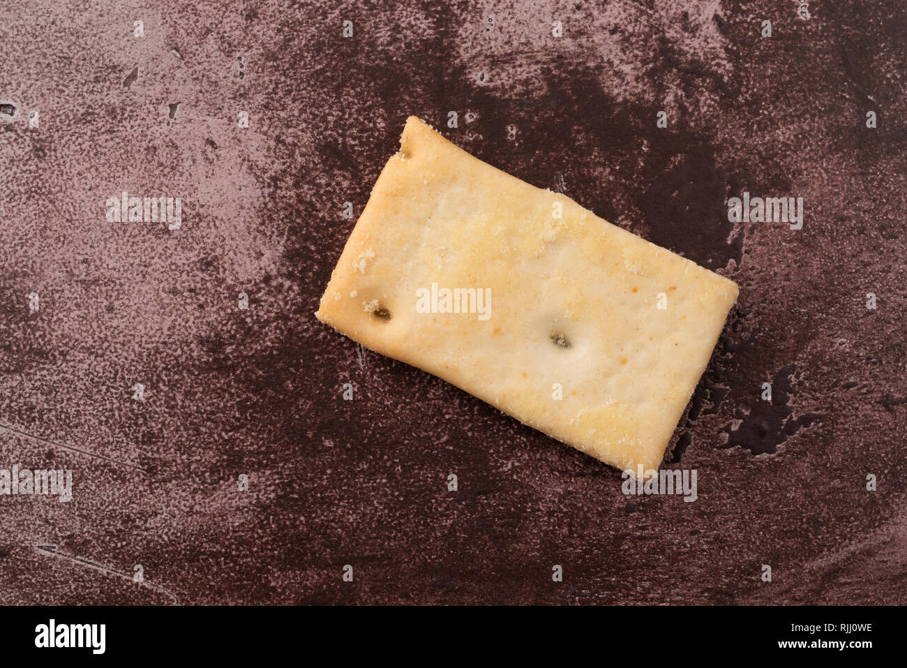Overhead view of a single cheese flavor crostini cracker on a maroon ...