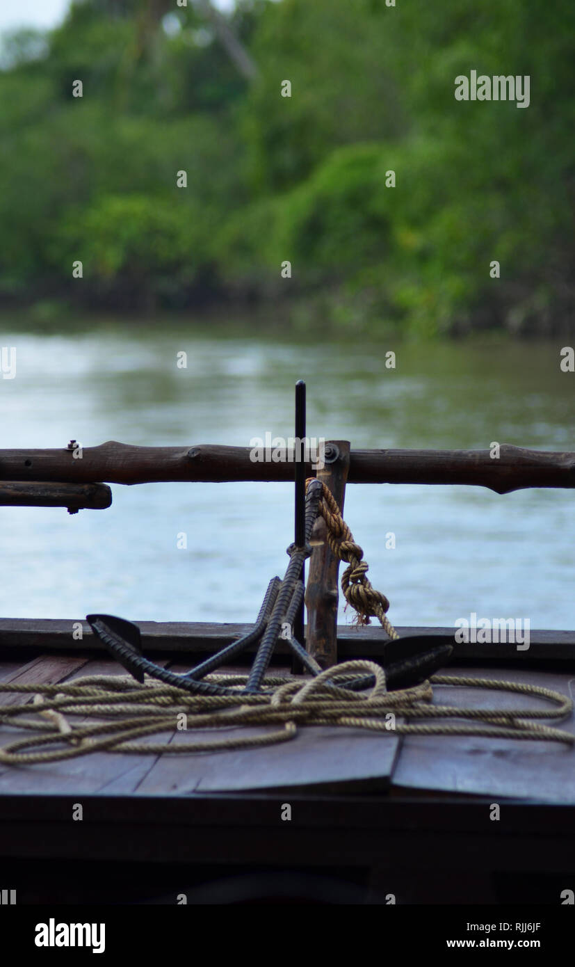 An anchor and rope rest on the back of a boat made from dark wood. A ...