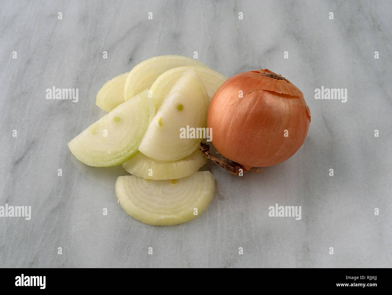 Side view of a whole yellow onion and one cut in slices on a gray ...