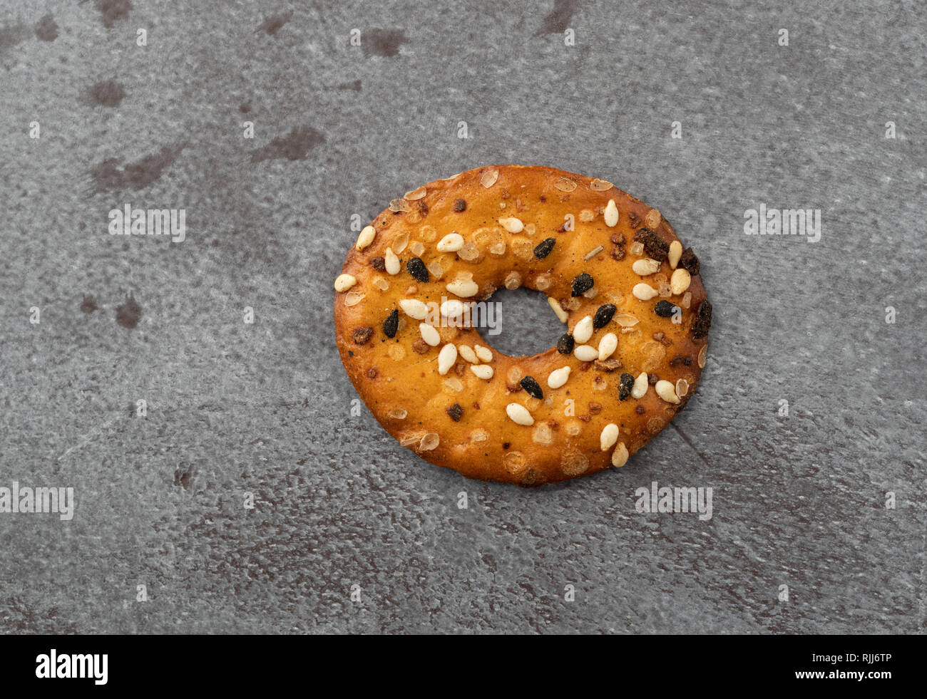 Top view of a single bite size bagel chip with assorted seeds on a gray ...