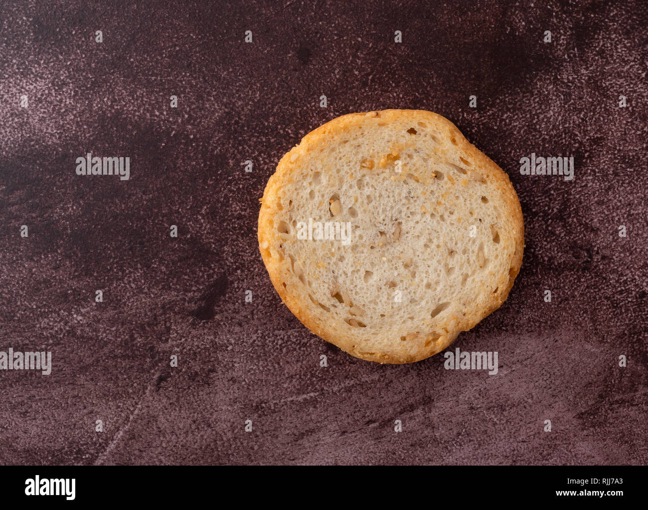 Overhead view of a single sesame round melba toast on a maroon ...