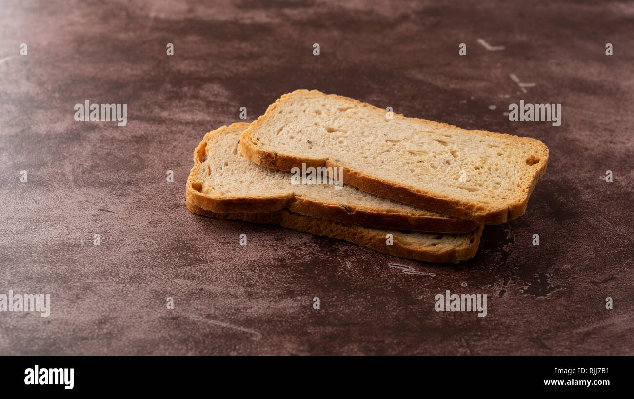 Side view of three slices of rye melba toast on a maroon background ...