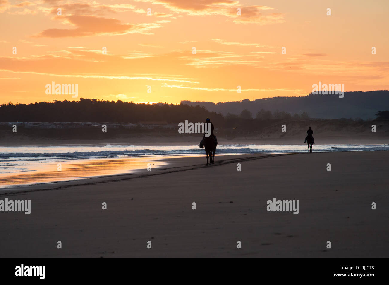 Silhouette of two horse riders on a beach at sunrise. Somo, Spain Stock ...
