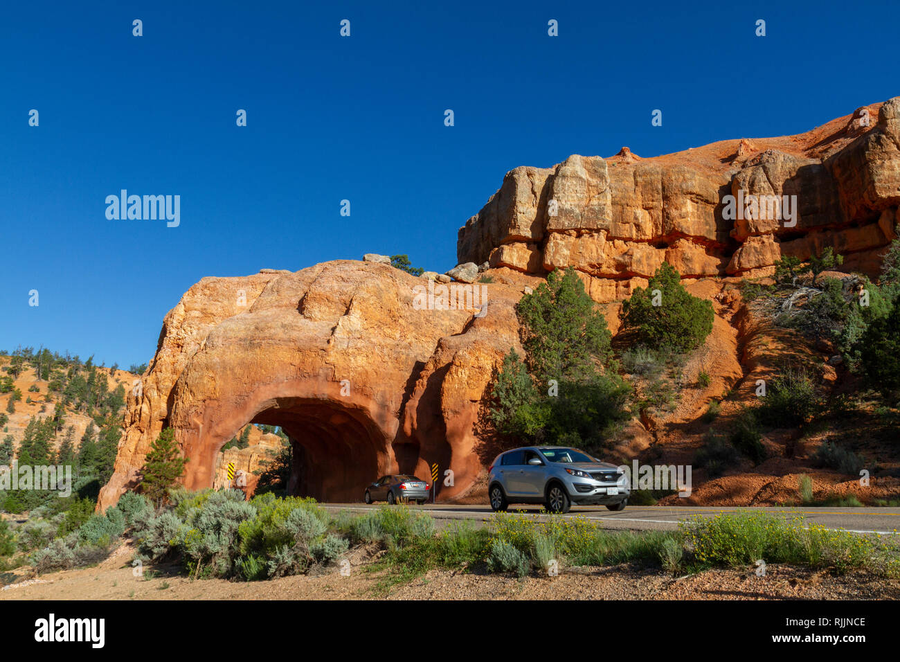 Car passing one of the Red Canyon Arches on Utah State Route 12 in the ...
