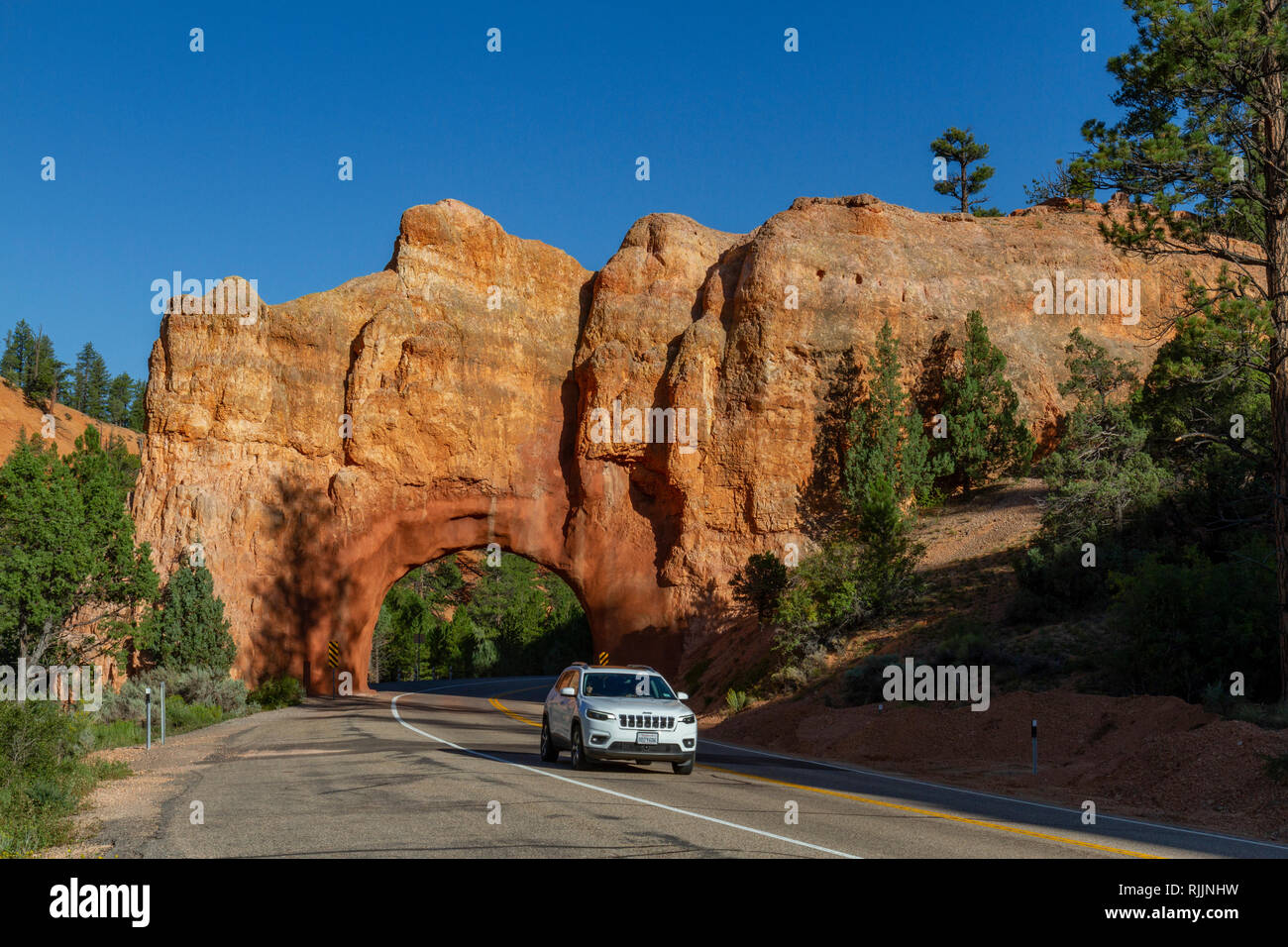 Car passing one of the Red Canyon Arches on Utah State Route 12 in the ...