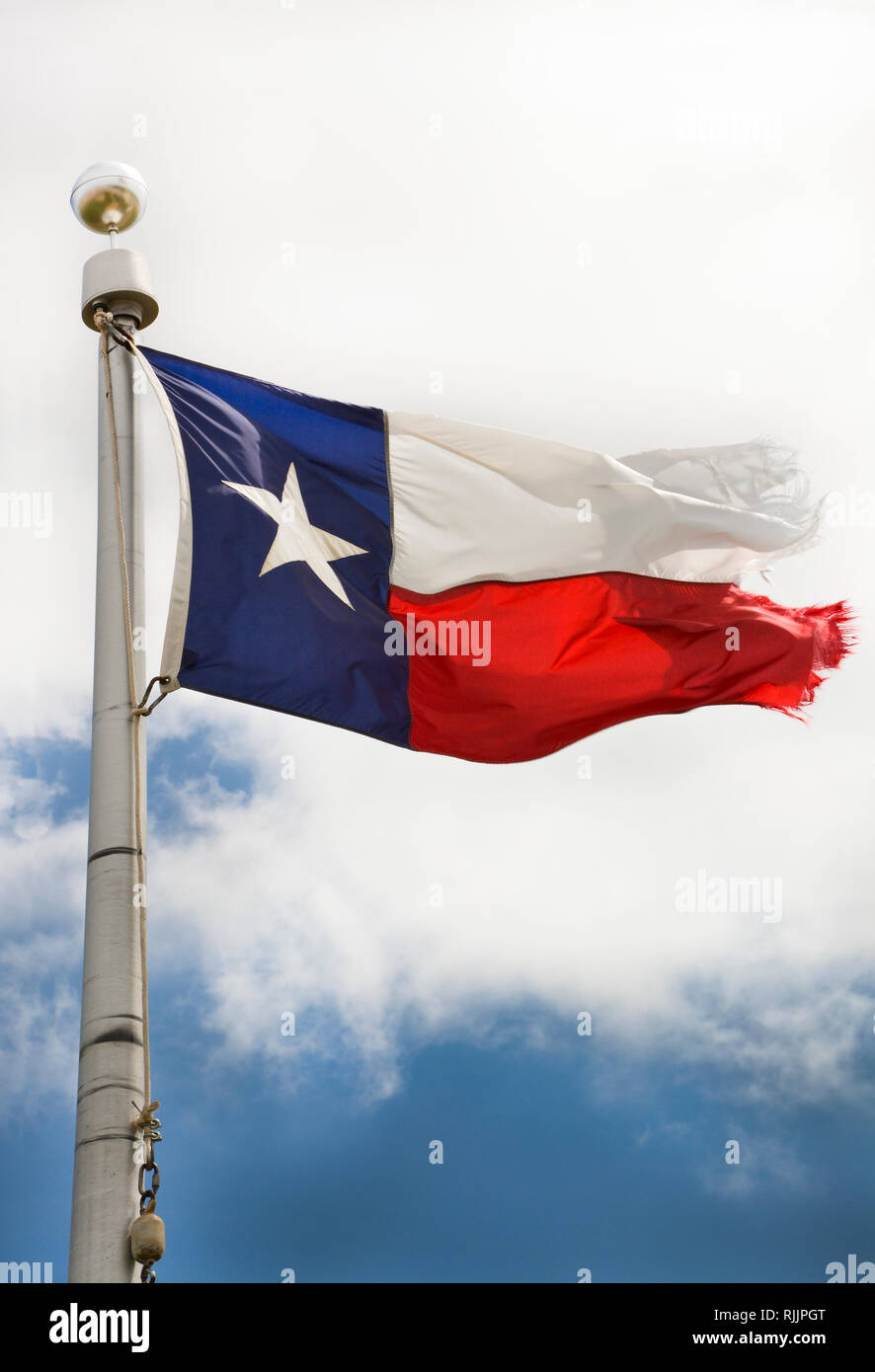 A tattered Texas State Flag waves on it's flag pole against the sky ...