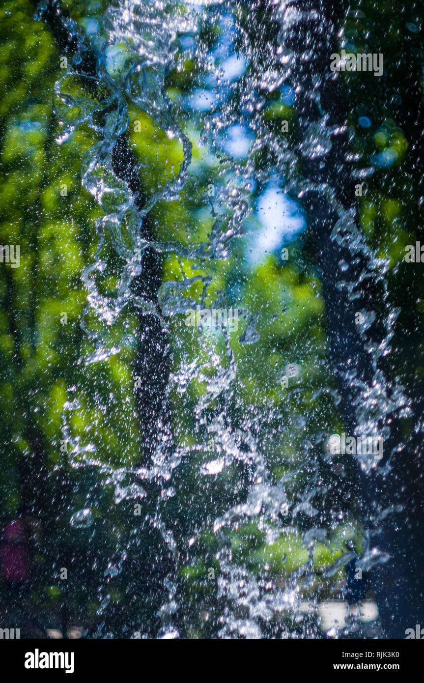 transparent falling water vertical flows against a blue sky and green ...