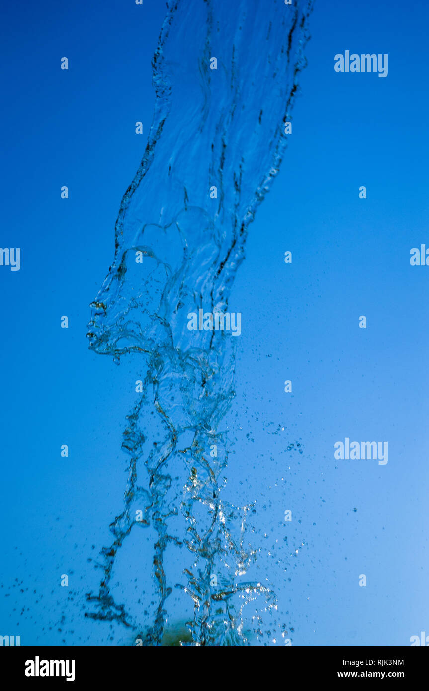 transparent falling water vertical flows against a blue sky and green ...
