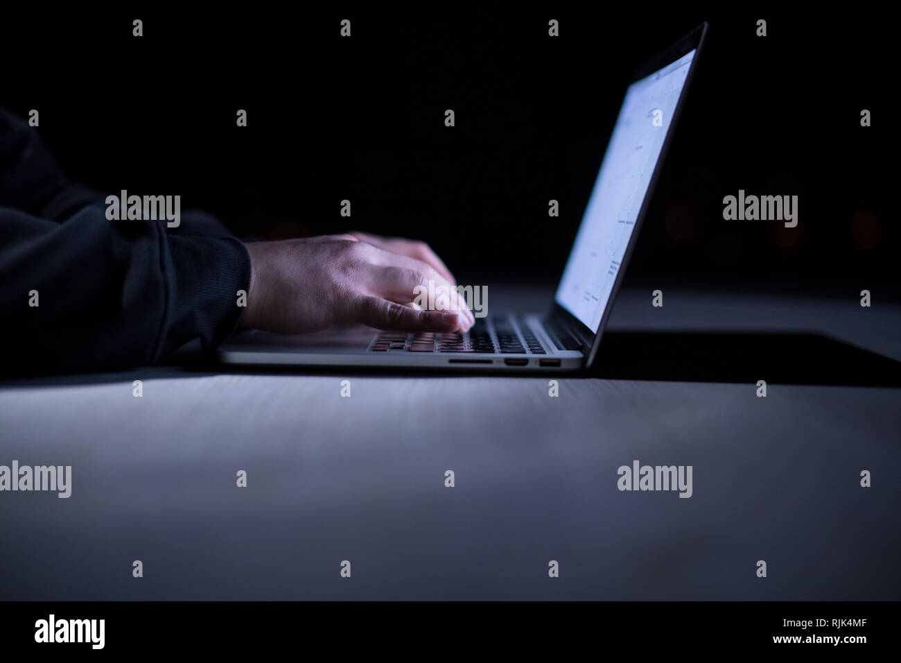 Young talented hacker using laptop computer while working in dark ...