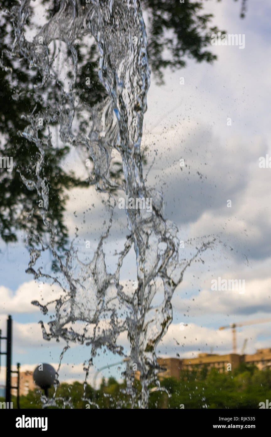 transparent falling water vertical flows against a blue sky and green ...