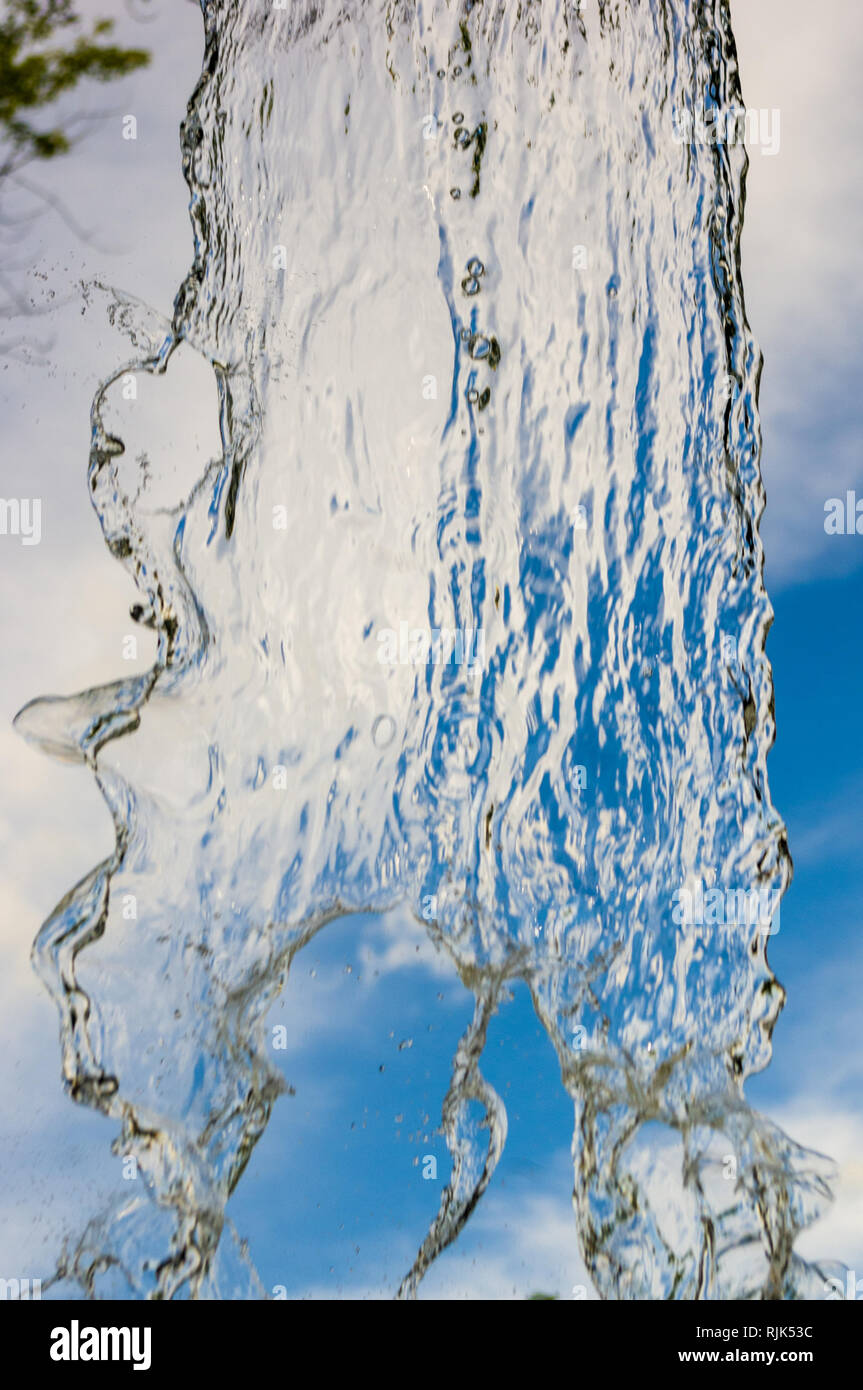 transparent falling water vertical flows against a blue sky and green ...