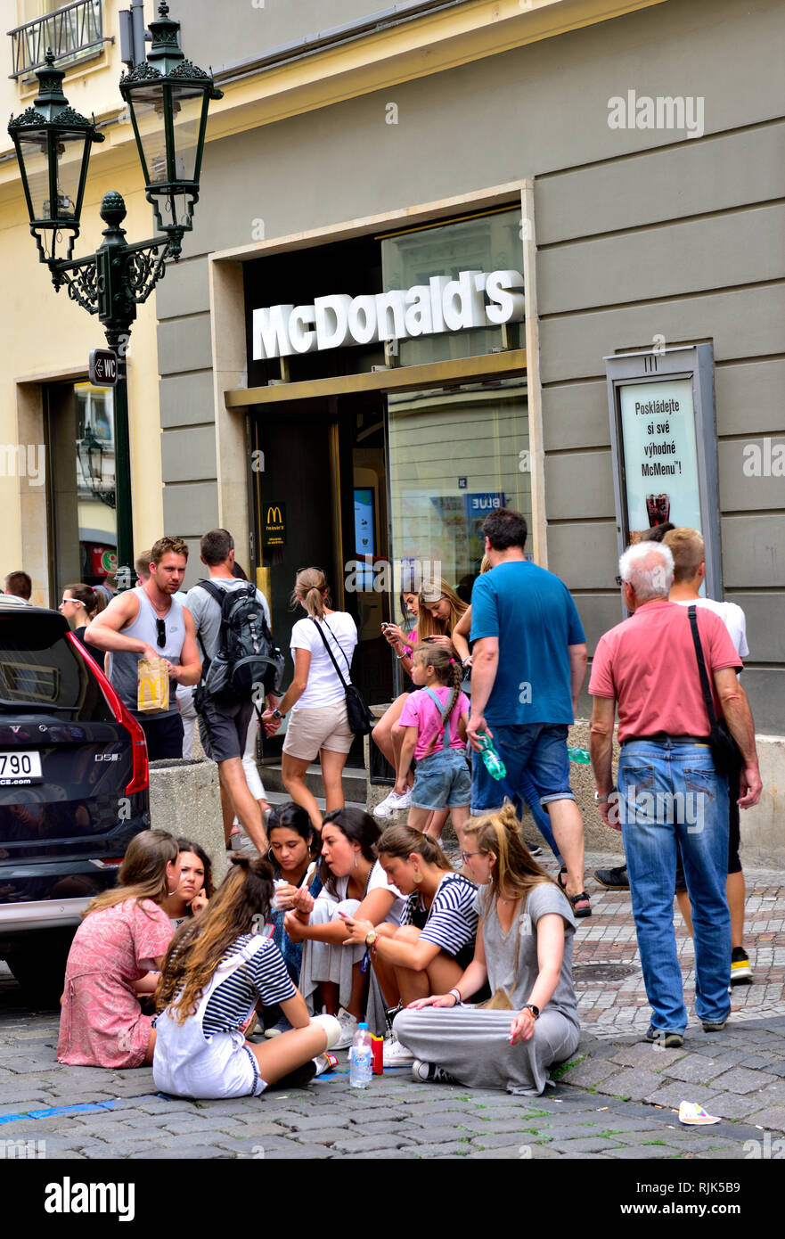 People sitting on pavement and road outside McDonald's in Prague eating ...